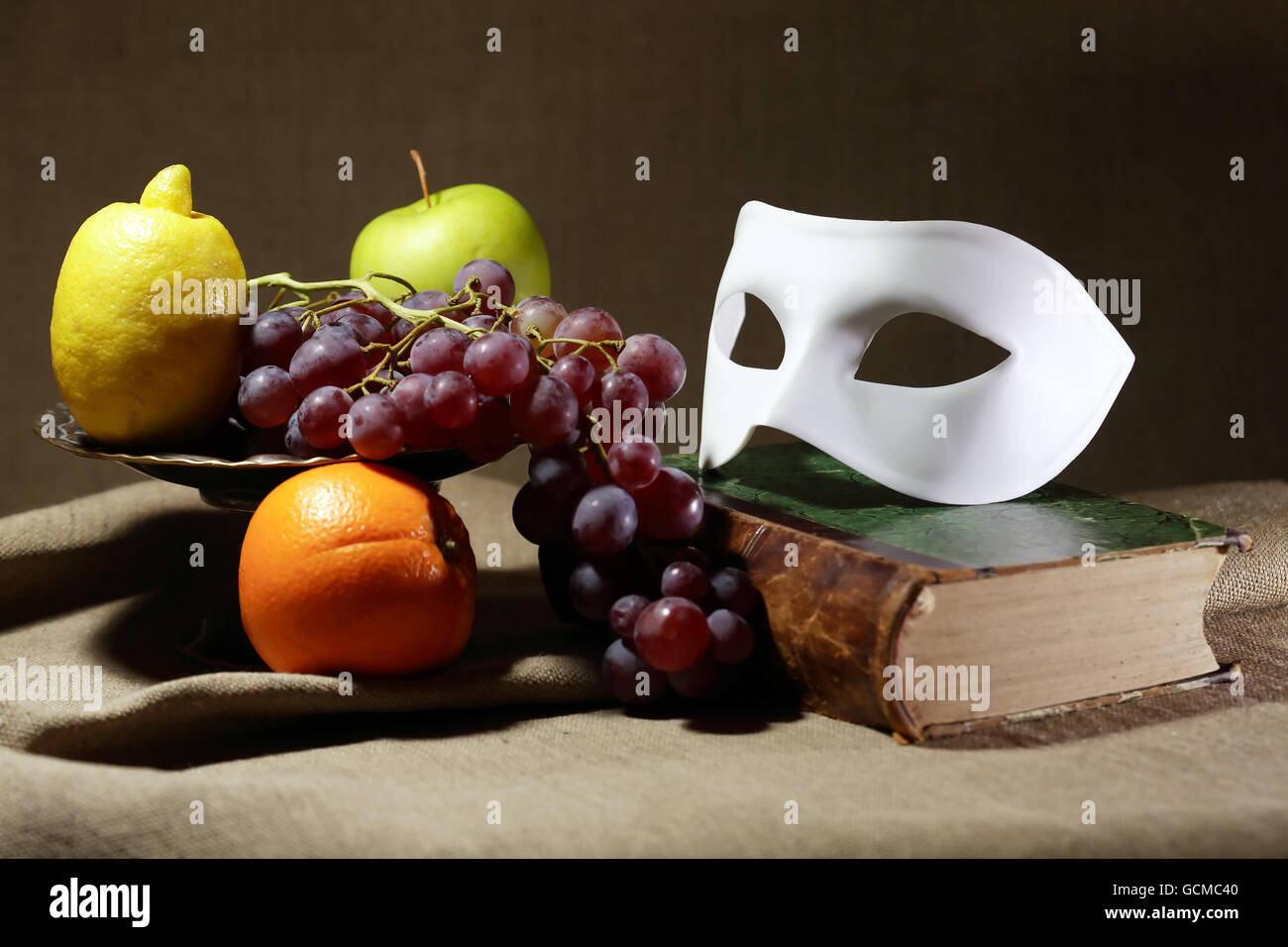 Vintage still life with mask on book near fruit bowl Stock Photo - Alamy
