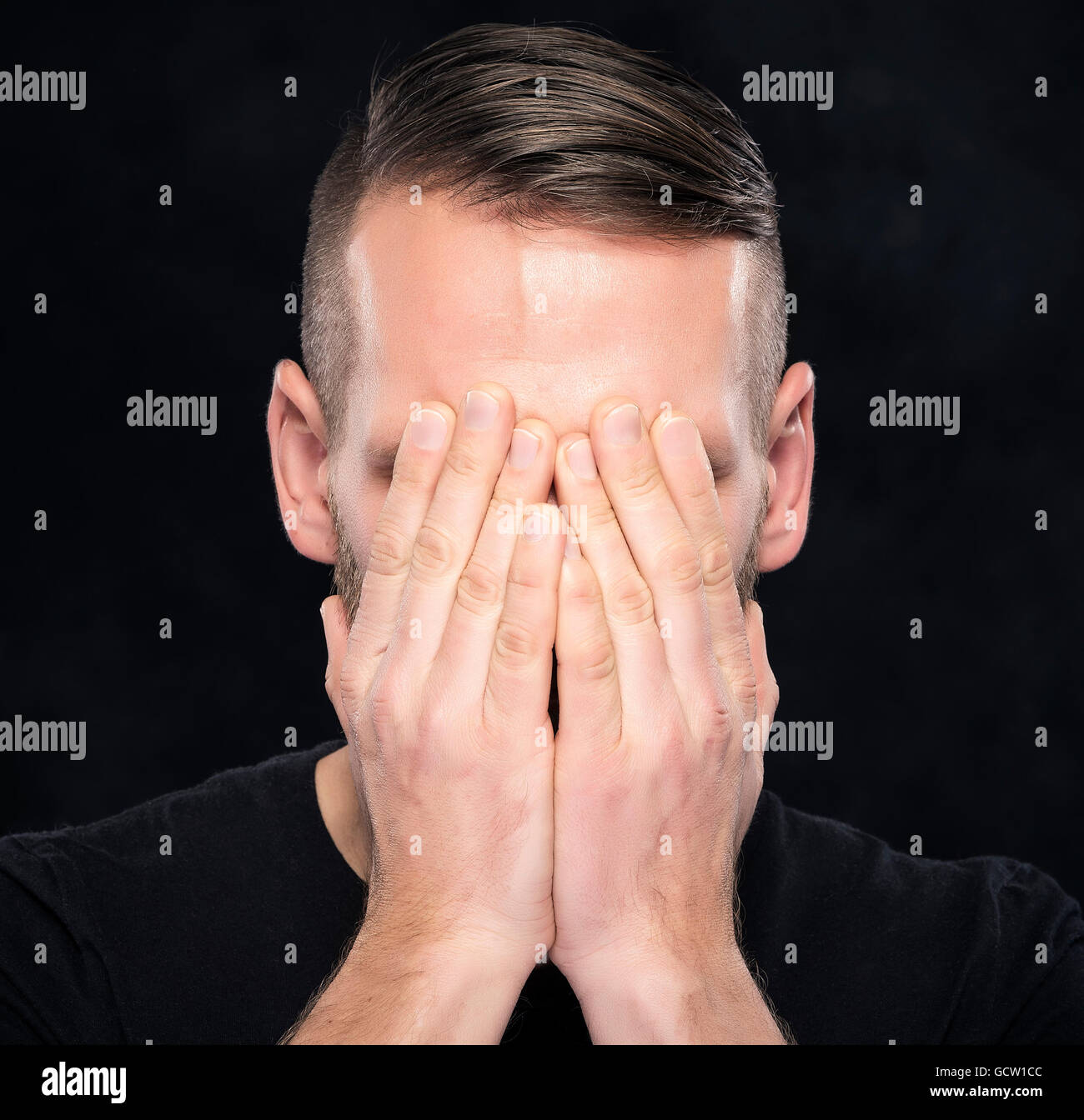 Man covers face with hands on dark background Stock Photo - Alamy