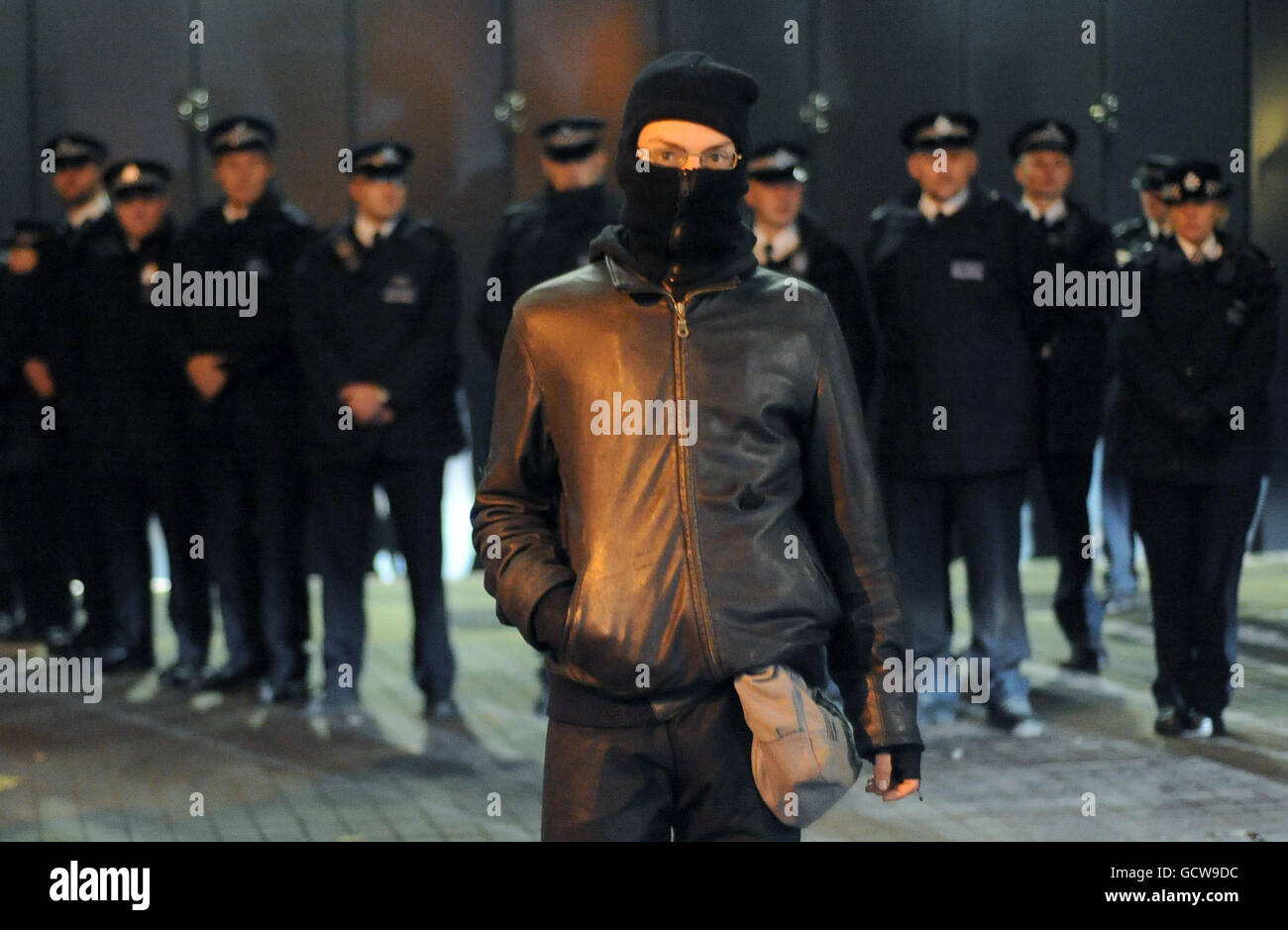 A masked demonstrator is seen in front of police officers as students ...