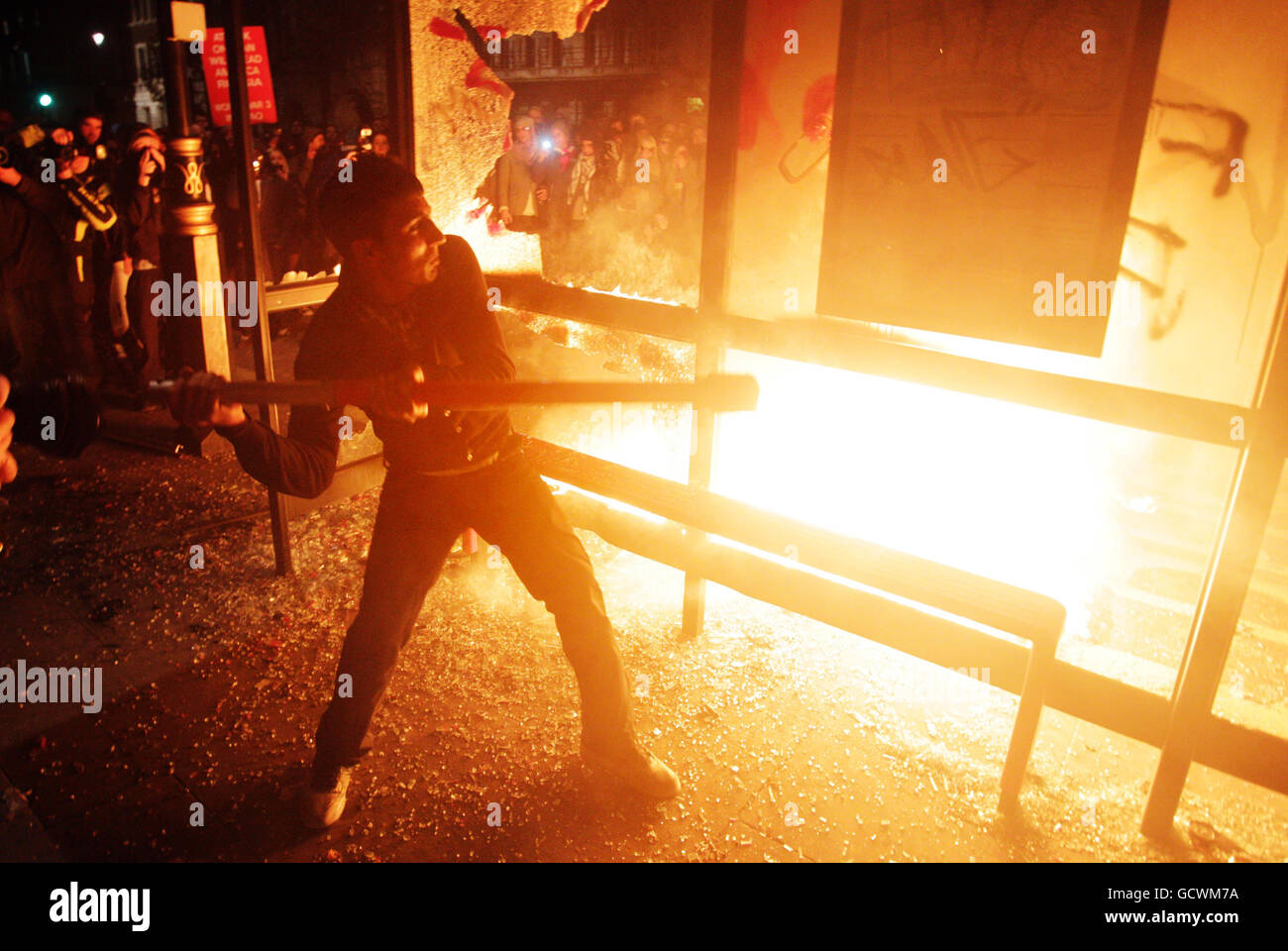 A protester smashes a burning bus shelter during a demonstration ...