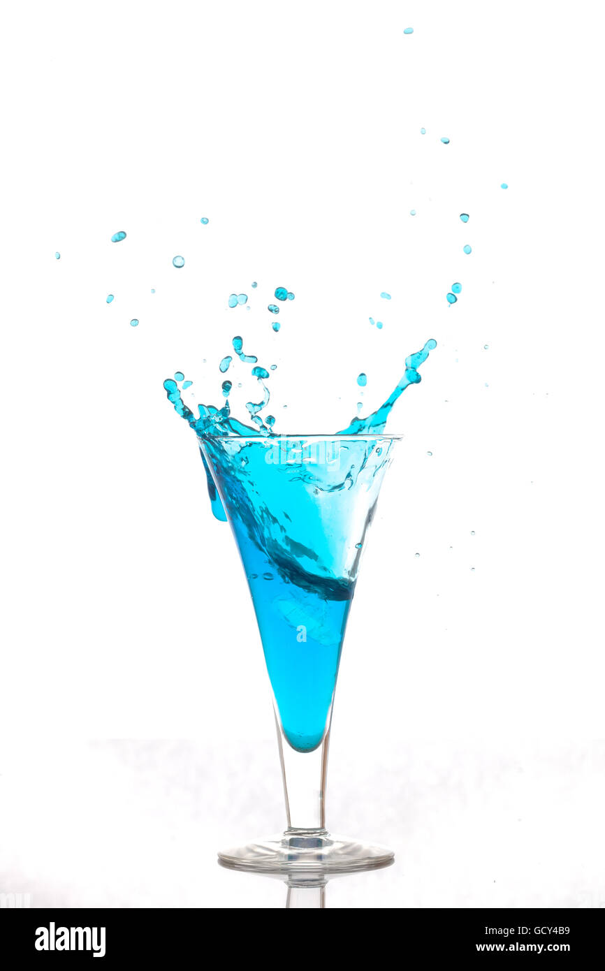 an ice cube falling into an blue alcoholic beverage splashing into the ...