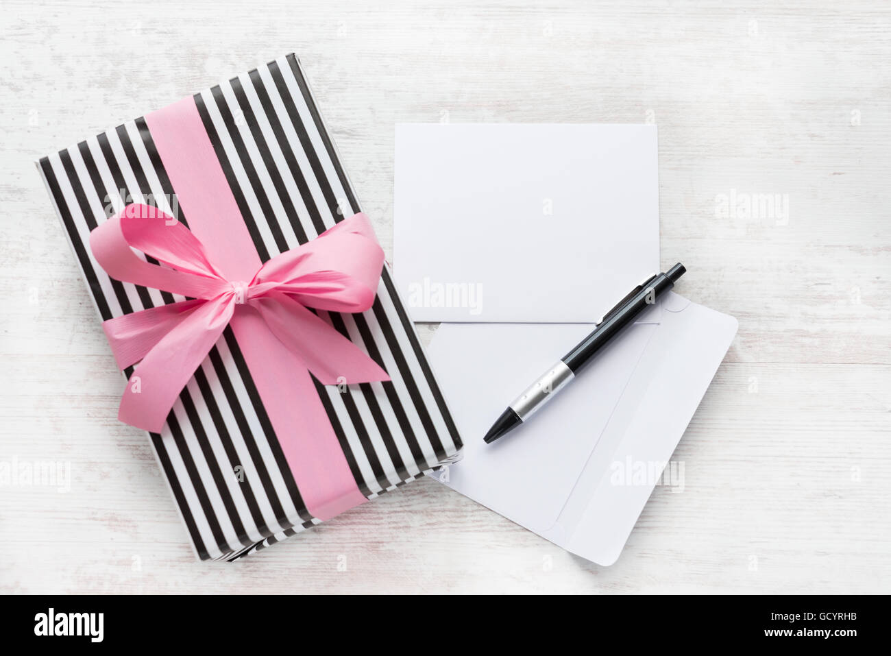 Empty greeting card. Wrapped gift, envelope and pen on a white wood ...