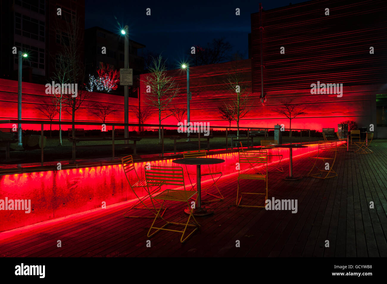 Downtown park at night with bright red colors and tables and metal ...