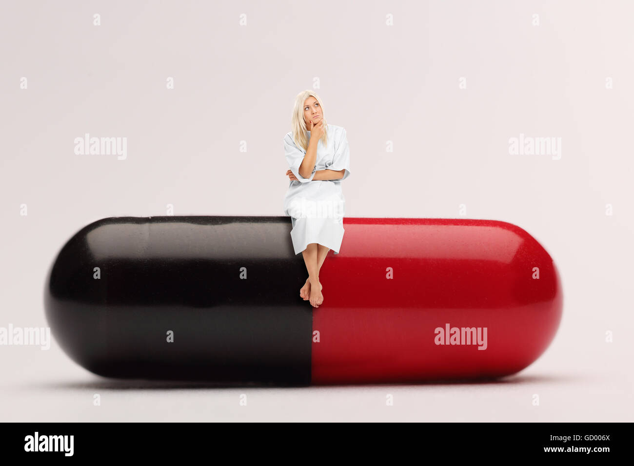 Pensive female patient sitting on a giant pill and looking in the ...