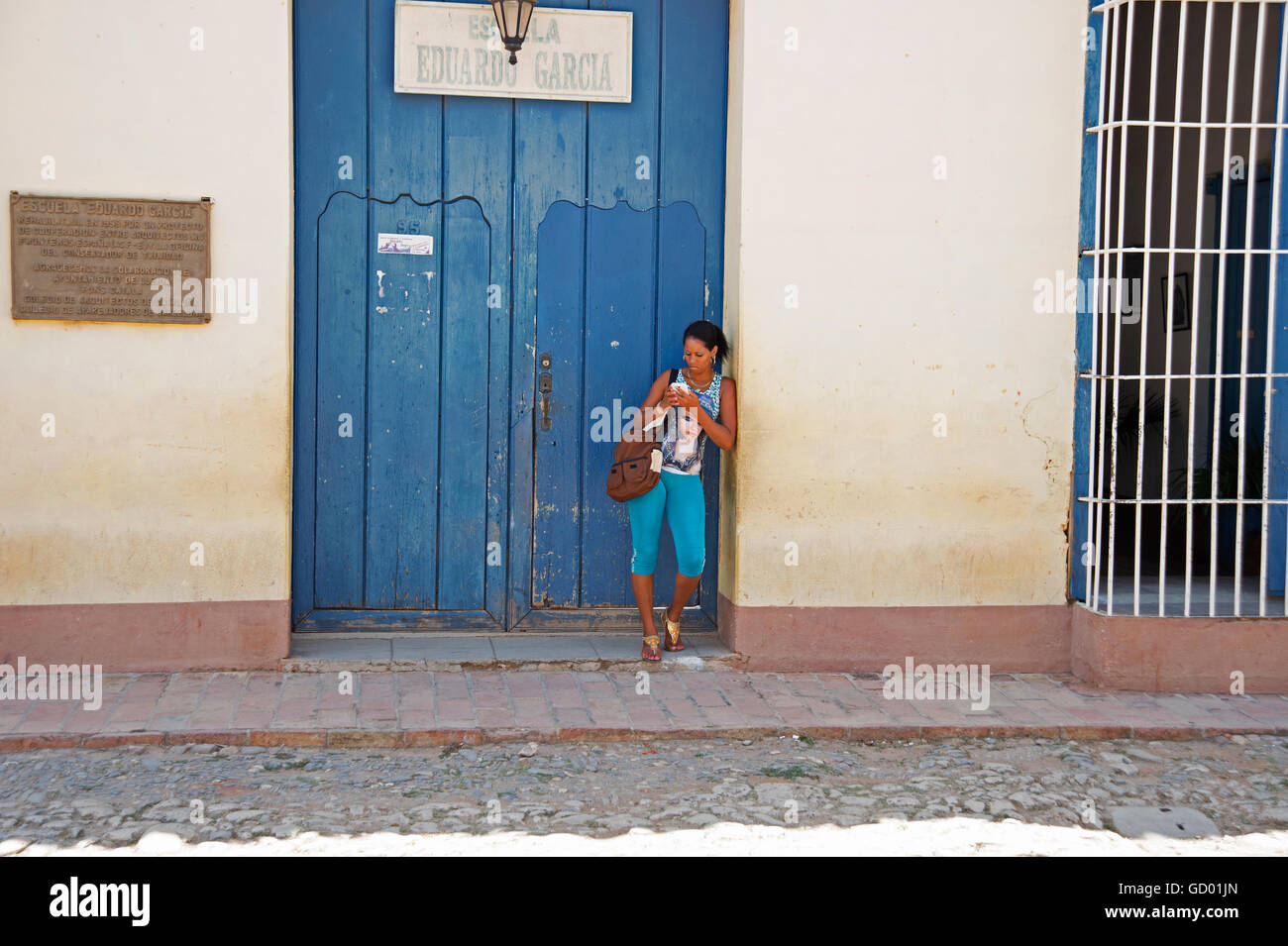 A young Cuban woman checking her mobile phone in a Trinidad doorway ...