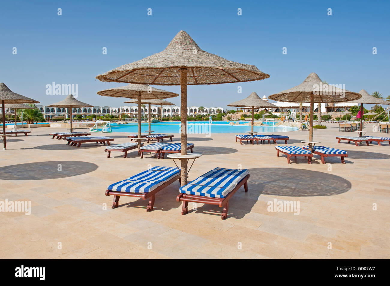 Sunbeds and wicker parasol umbrellas round the side of a tropical hotel ...
