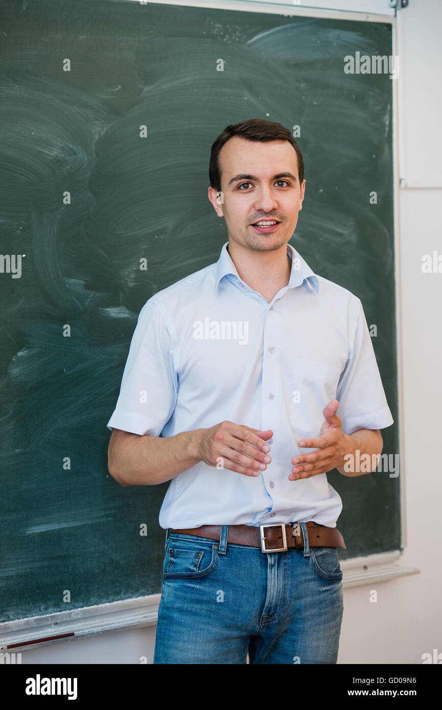Portrait of young handsome student or teacher in a class pointing at ...