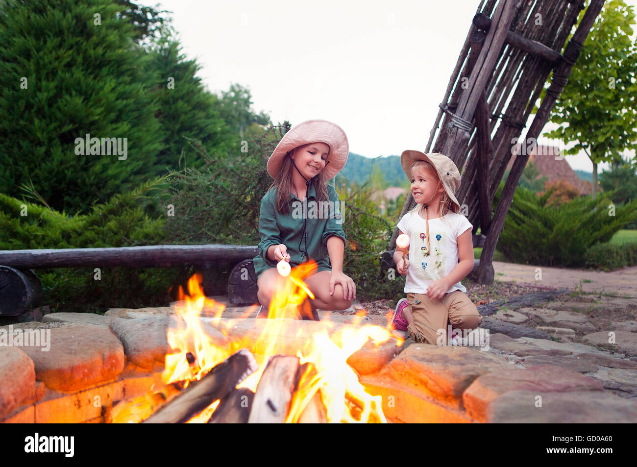 Two happy sisters roasting marshmallows on campfire in the evening ...