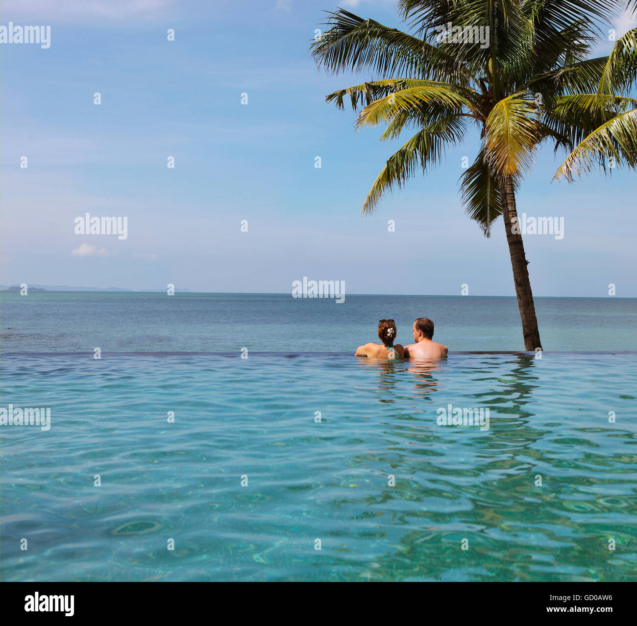 Young couple relaxing in infinity pool under coco palms in front of ...