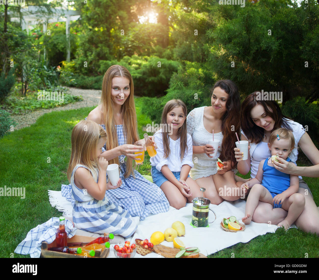 Three happy young mothers and daughters having picnic in summer park ...