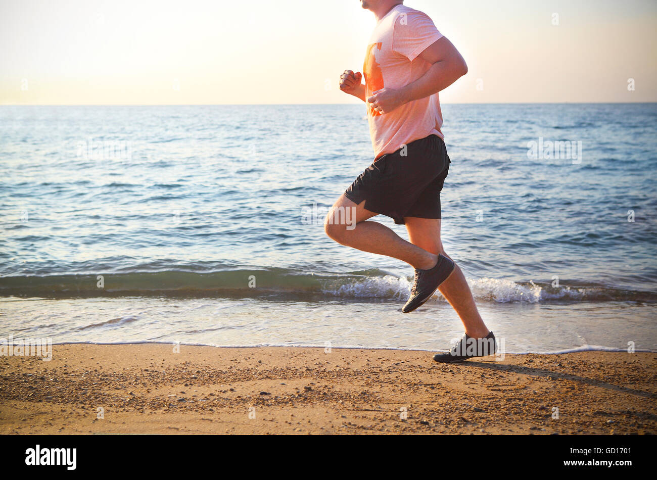 Young man running on the beach at sunset Stock Photo - Alamy