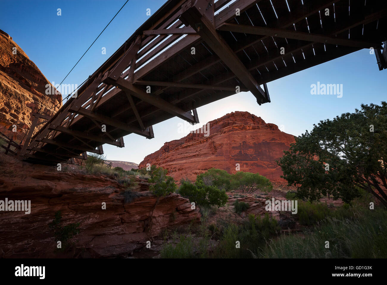 A footbridge spanning a canyon stream stretches overhead with tall, red ...