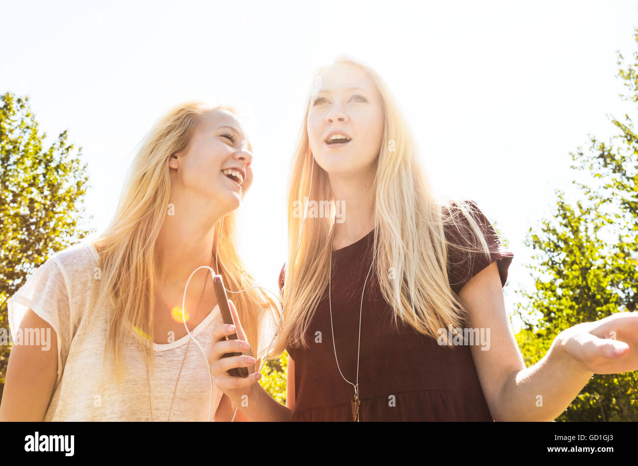 Two sisters having fun outdoors and singing together in a city park ...