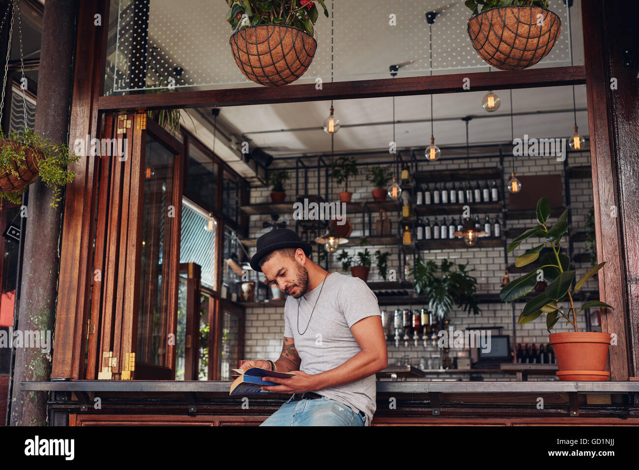 Portrait of relaxed young man sitting at a cafe counter reading a book ...