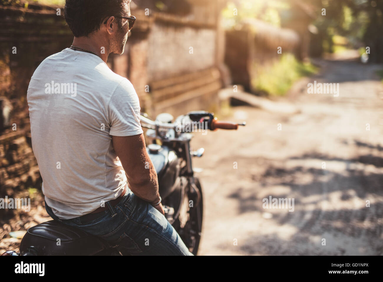 Rear view shot of young man sitting on his motorcycle and looking away ...