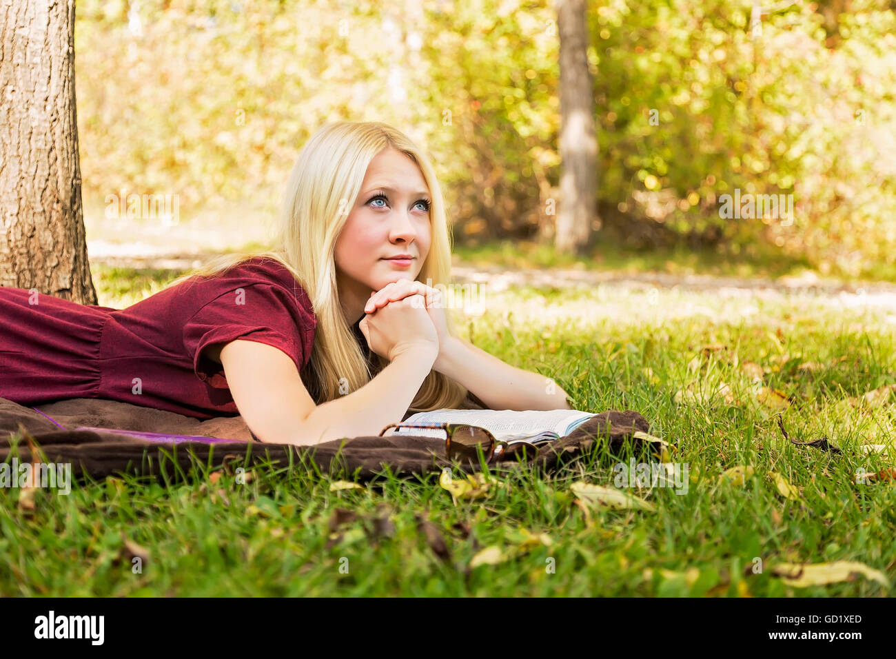 A young woman with long blond hair spending personal time in Bible study and praying outdoors in ...