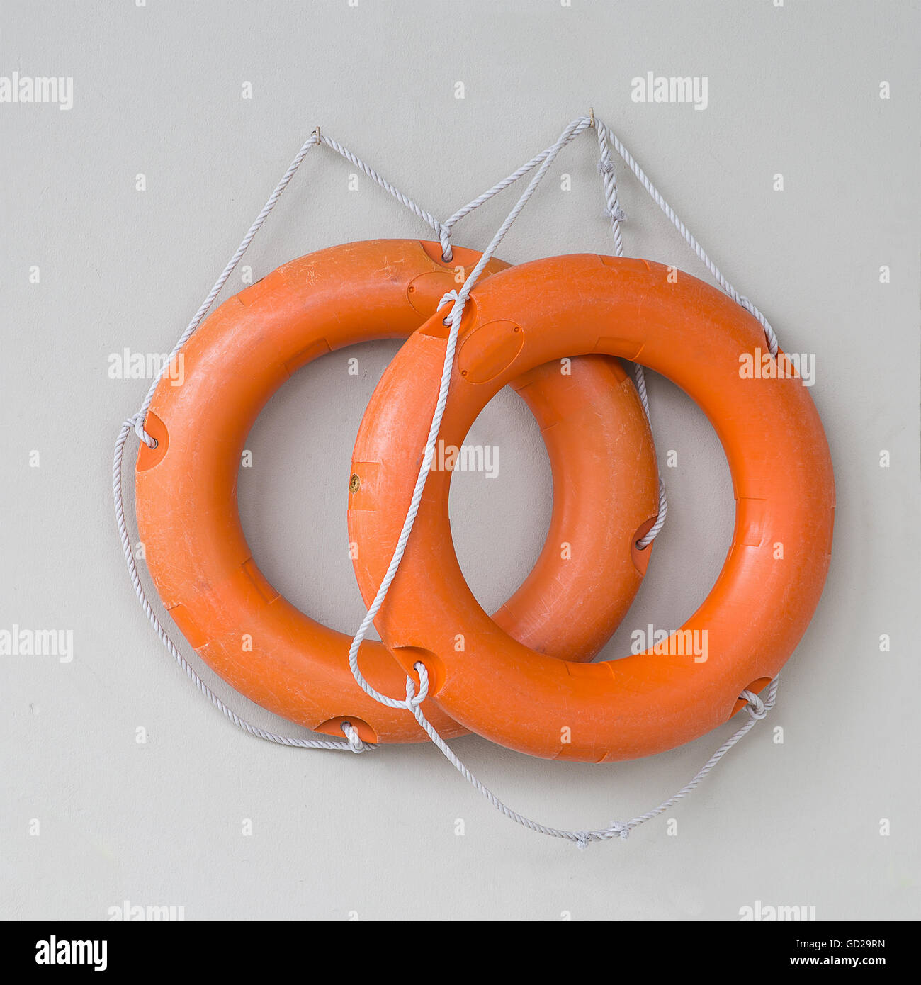 Two orange life rings with white rope hanging on gray wall near ...