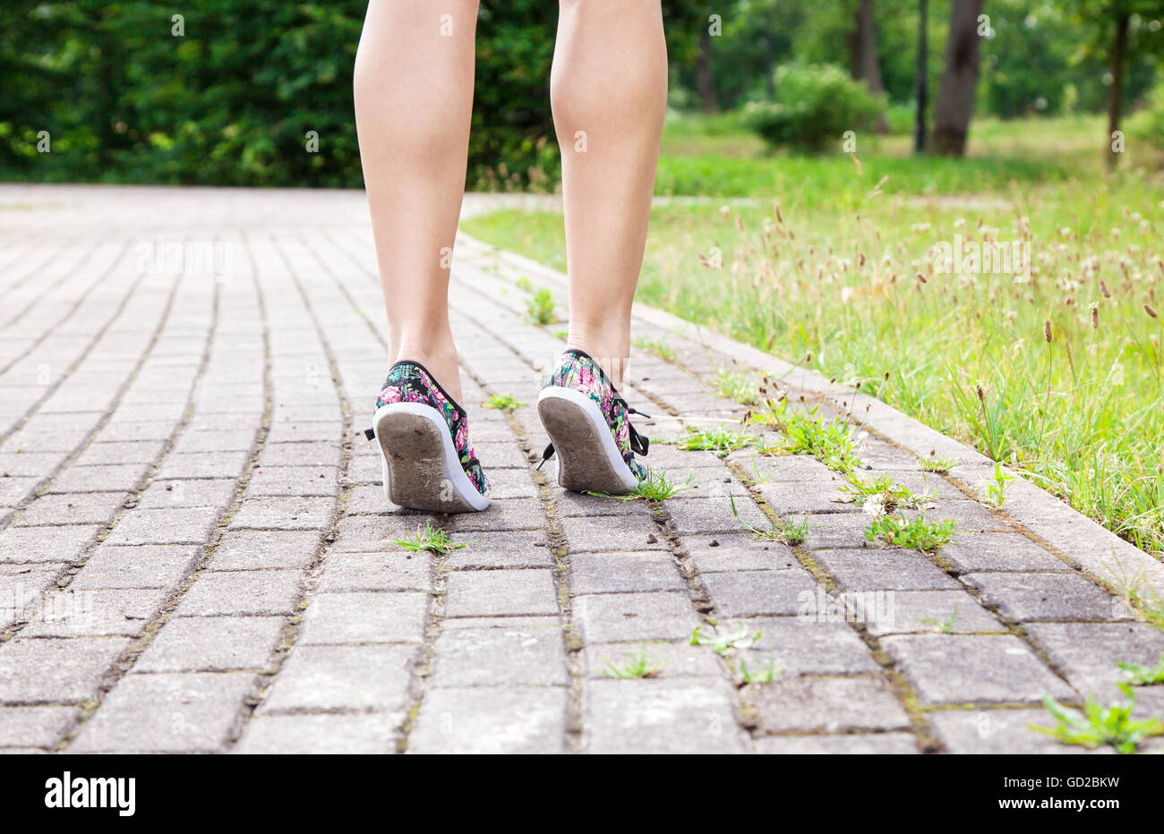 legs of a woman walking on the sidewalk in the park on summer day ...