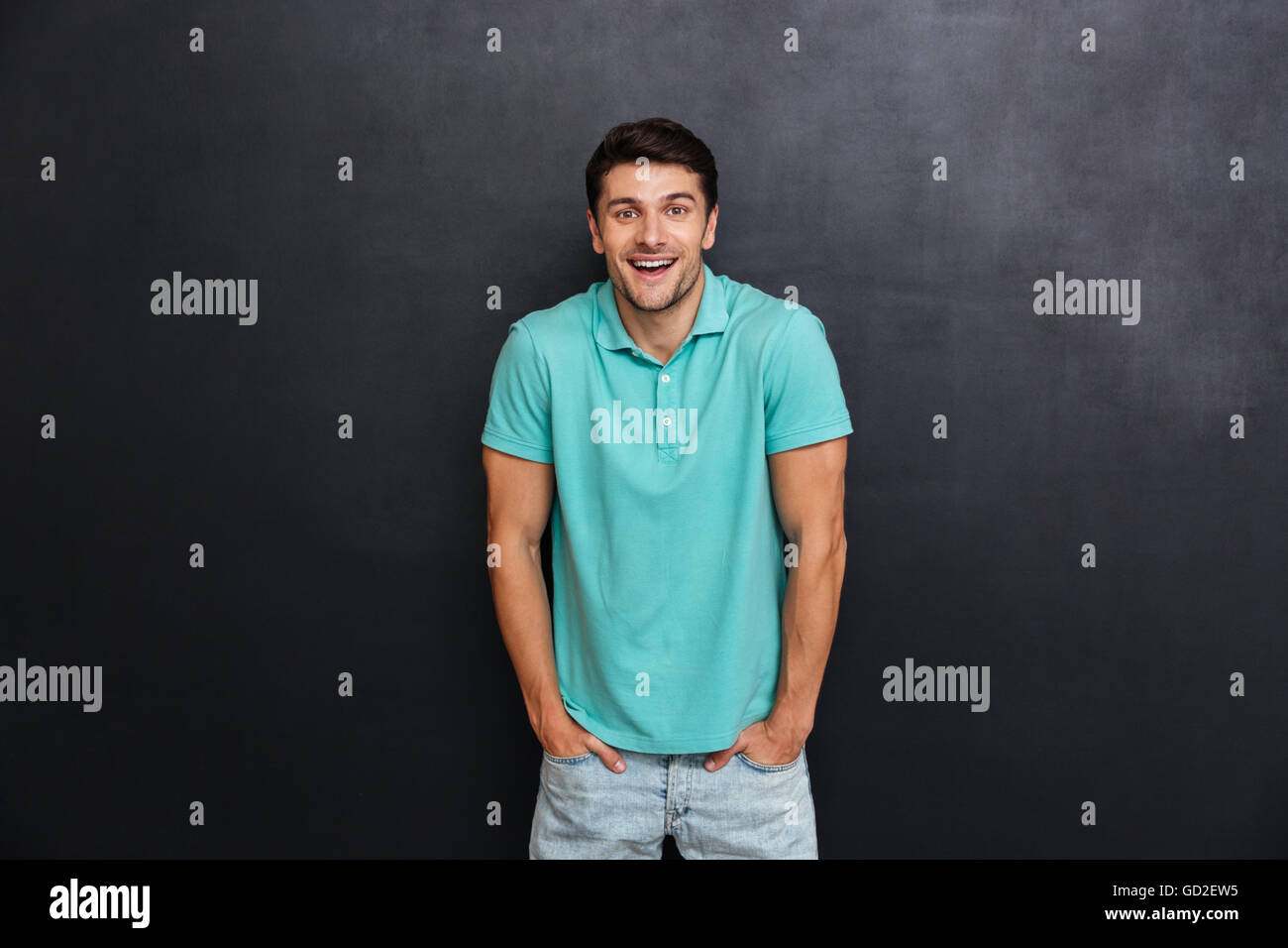 Cheerful excited young man standing with hands in pockets over ...