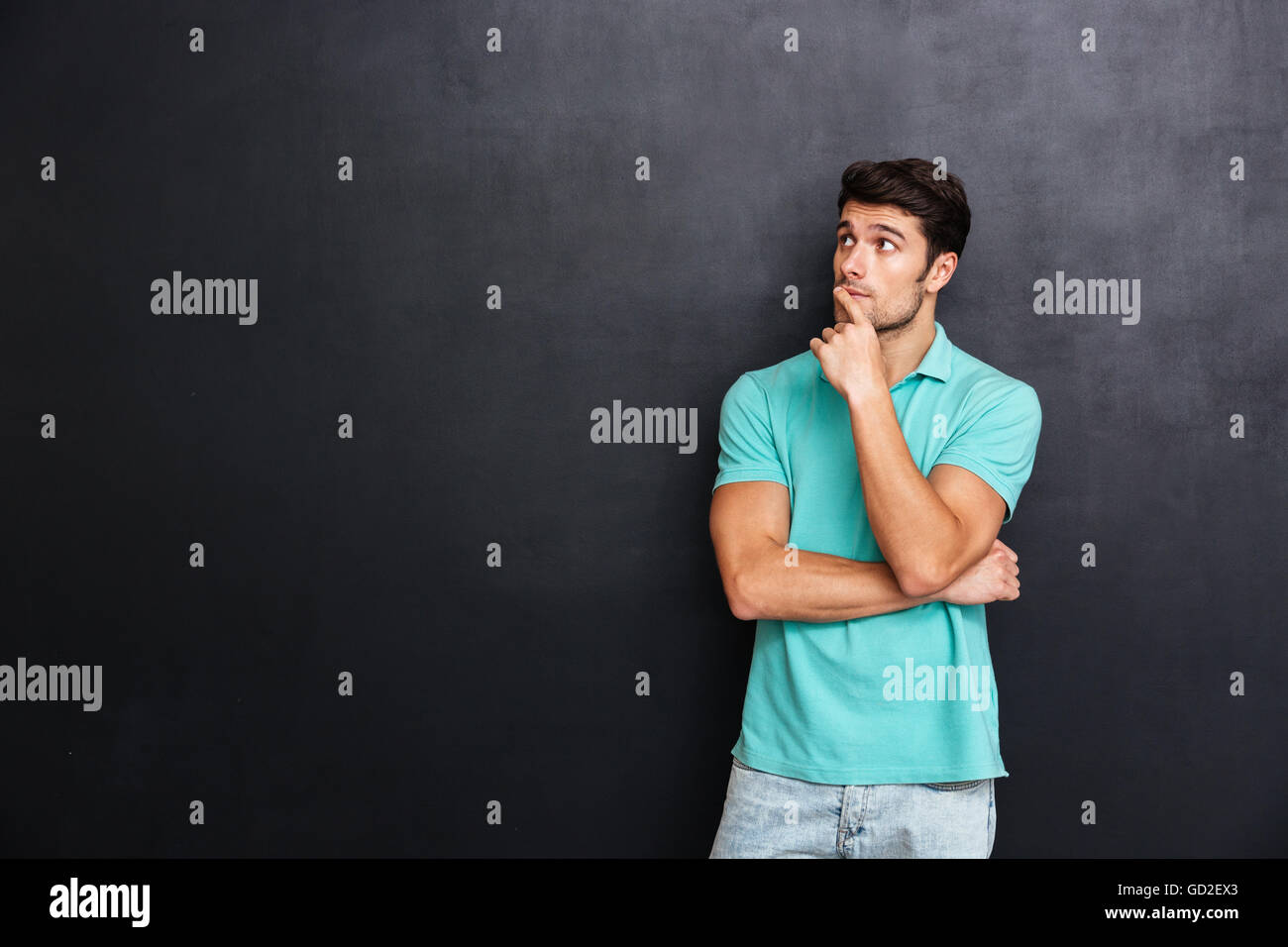 Pensive handsome young man standing with hands folded and thinking over ...
