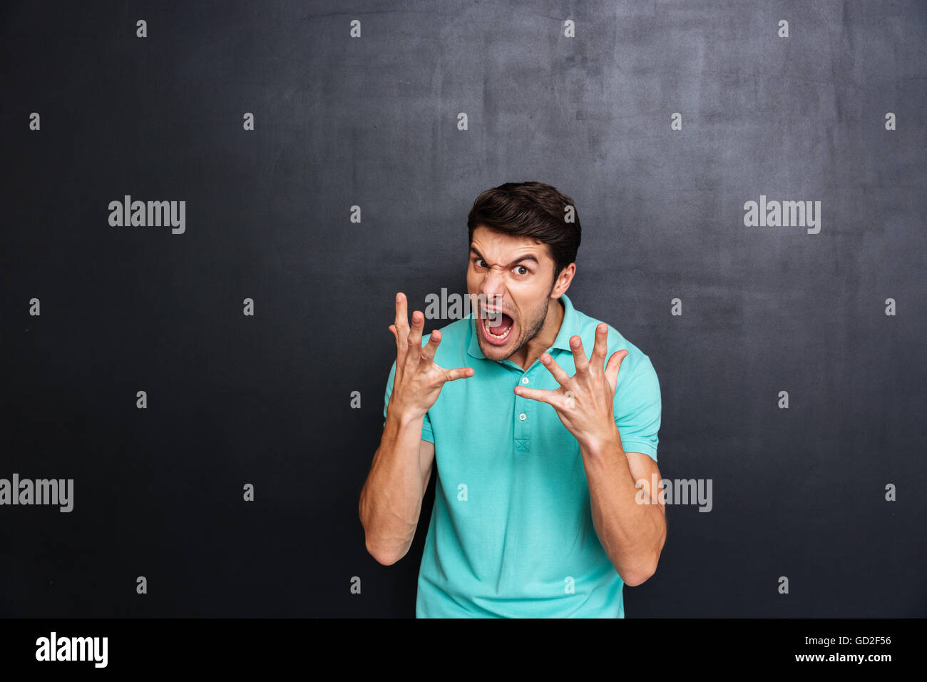 Mad furious young man standing and yelling over blackboard background ...
