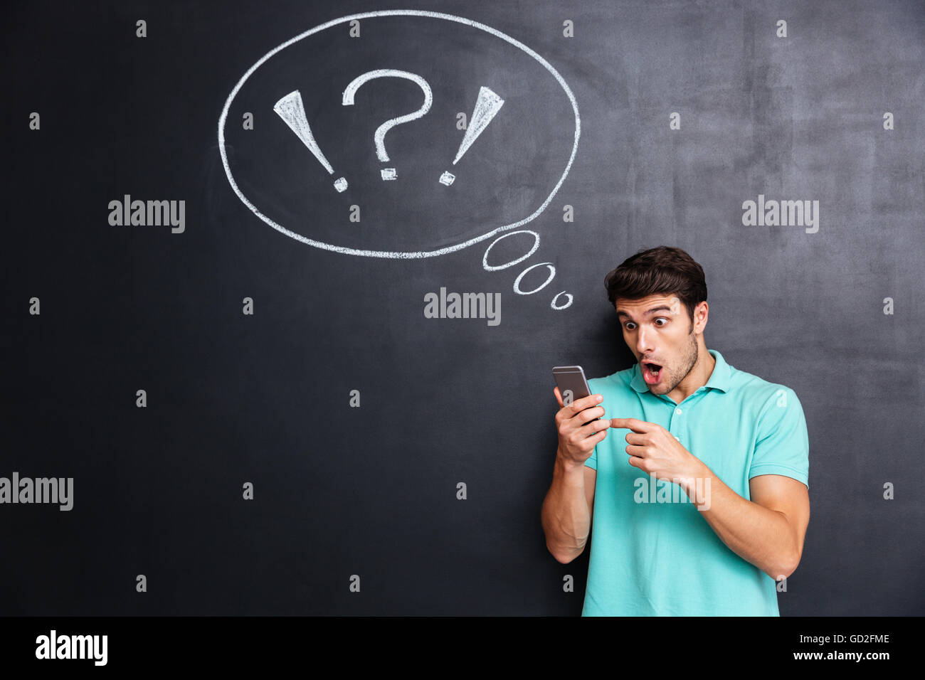 Shocked astonished young man using mobile phone over blackboard ...