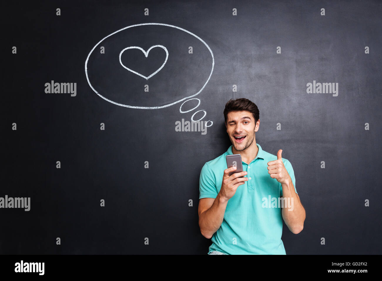 Cheerful young man in love using mobile phone and showing thumbs up ...