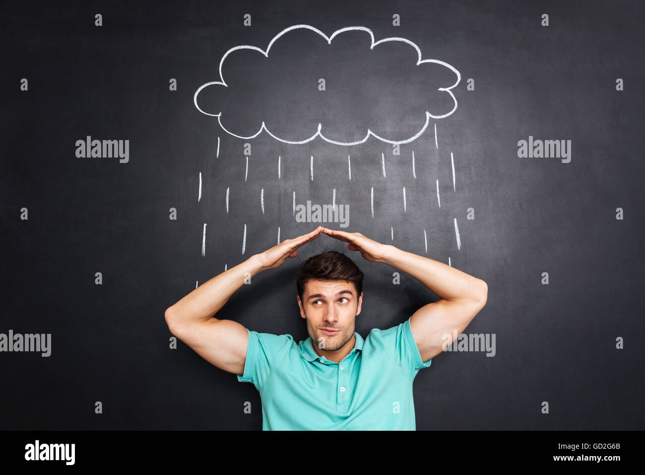 Unhappy young man imitating roof by hands and covering from drawn rain ...