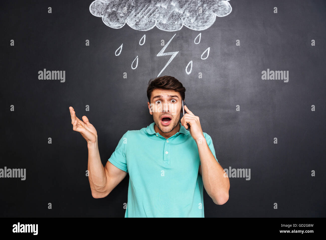 Confused angry young man standing with mobile phone on blackboard ...