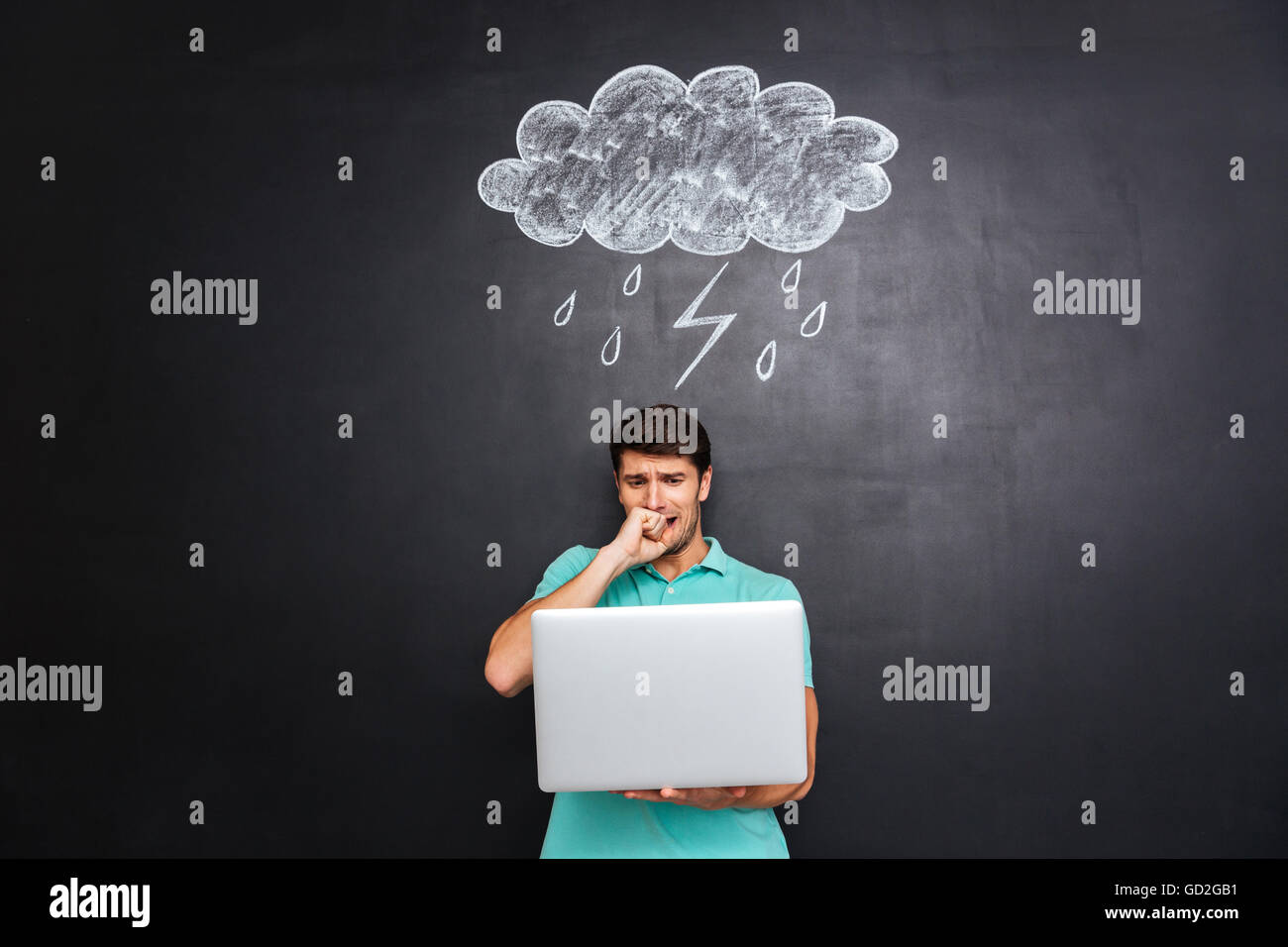 Nervous young man looking at pc computer with chalk blackboard behind ...