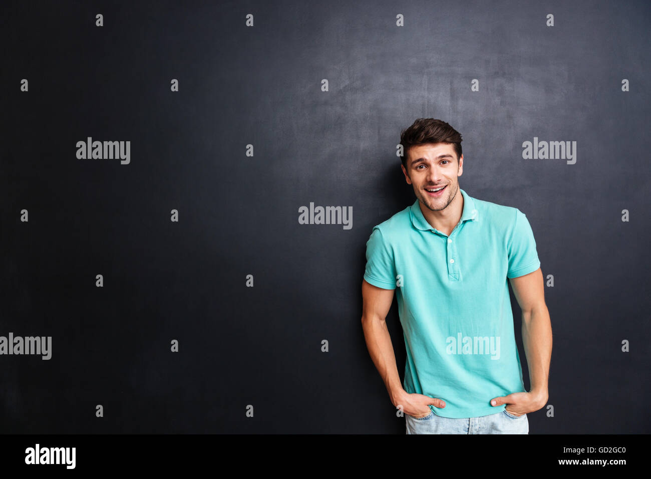 Handsome young smiling man looking at camera with hands in his pockets ...