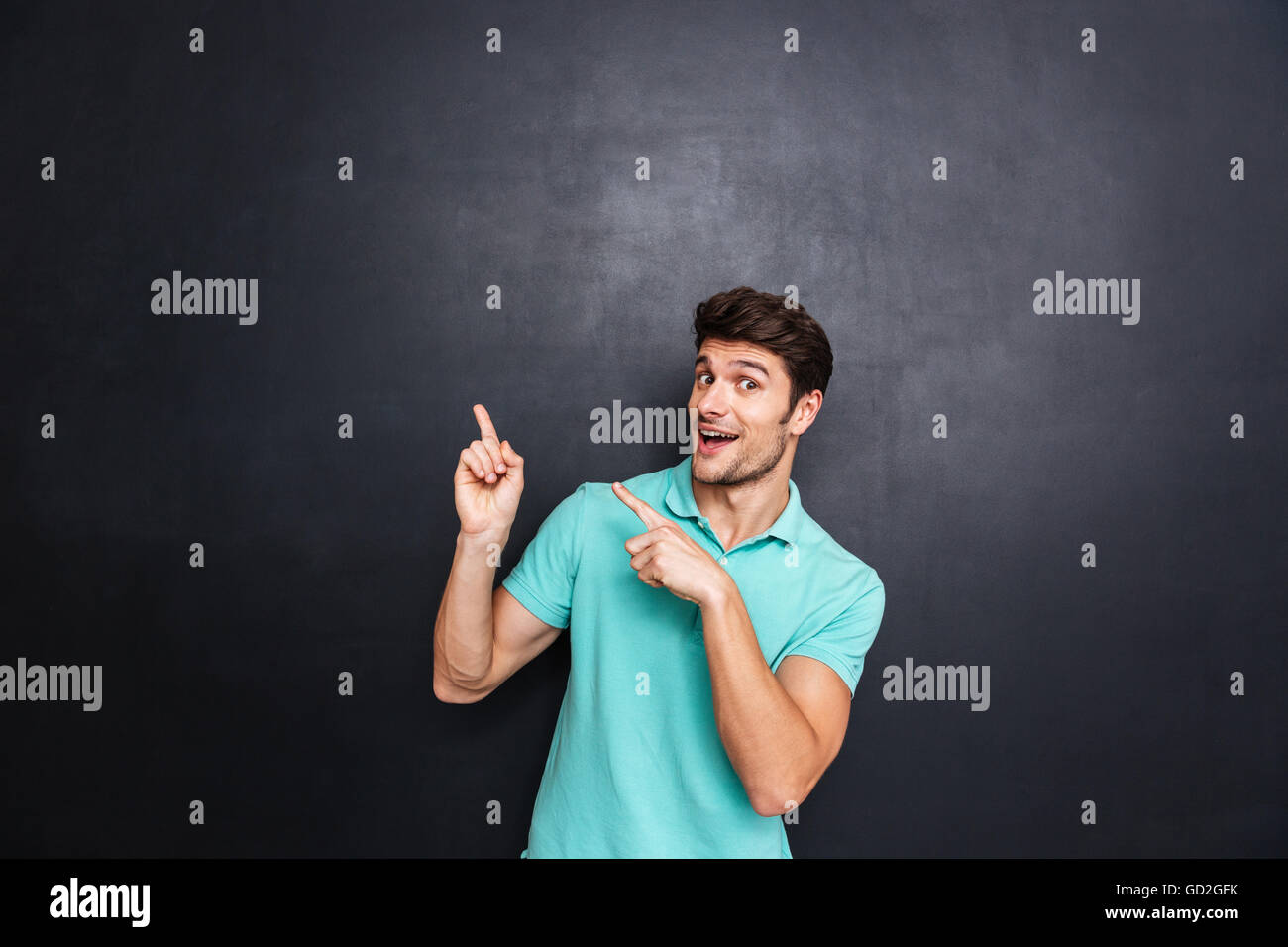 Smiling happy young man pointing fingers away with both hands over ...