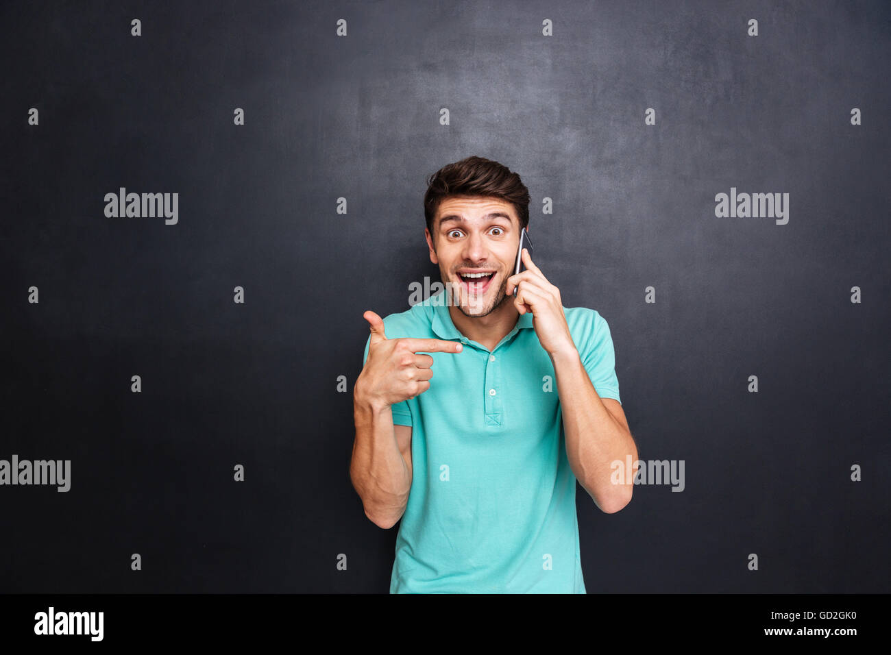 Happy excited young man talking on mobile phone and pointing on it over ...