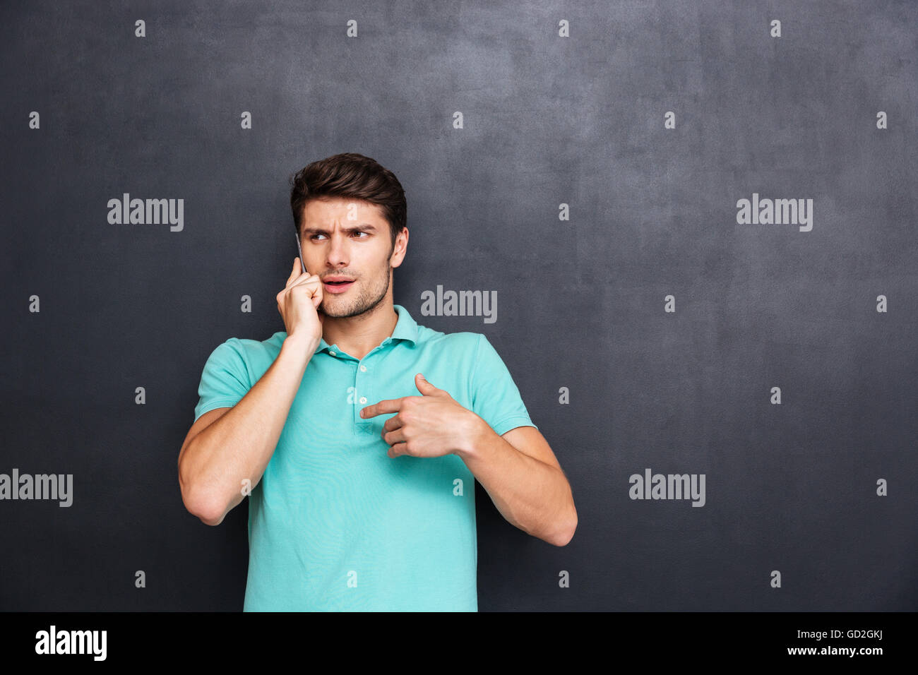 Confused handsome young man standing and talking on cell phone over ...