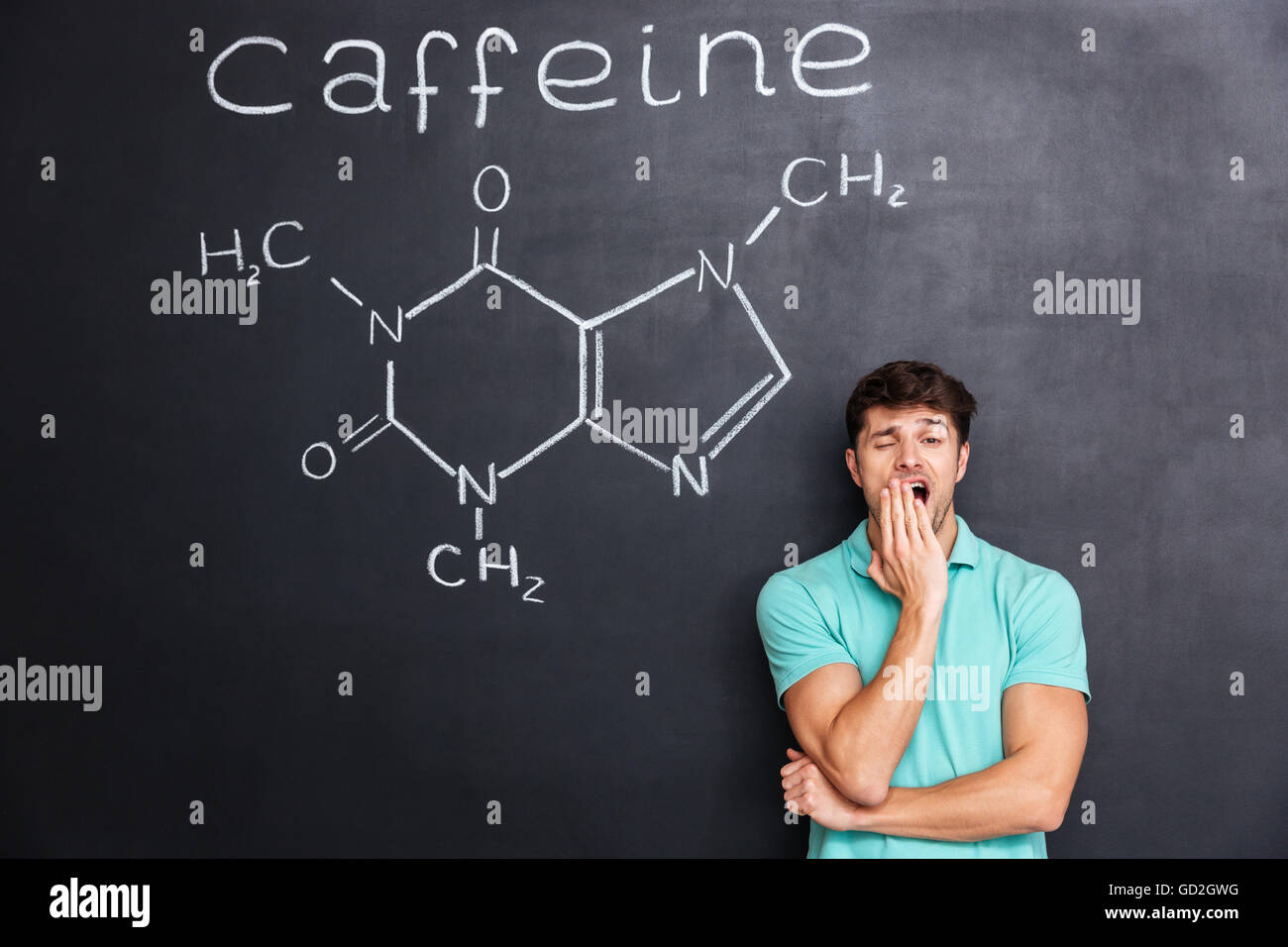Exhausted fatigued young man yawning over chalkboard background with ...