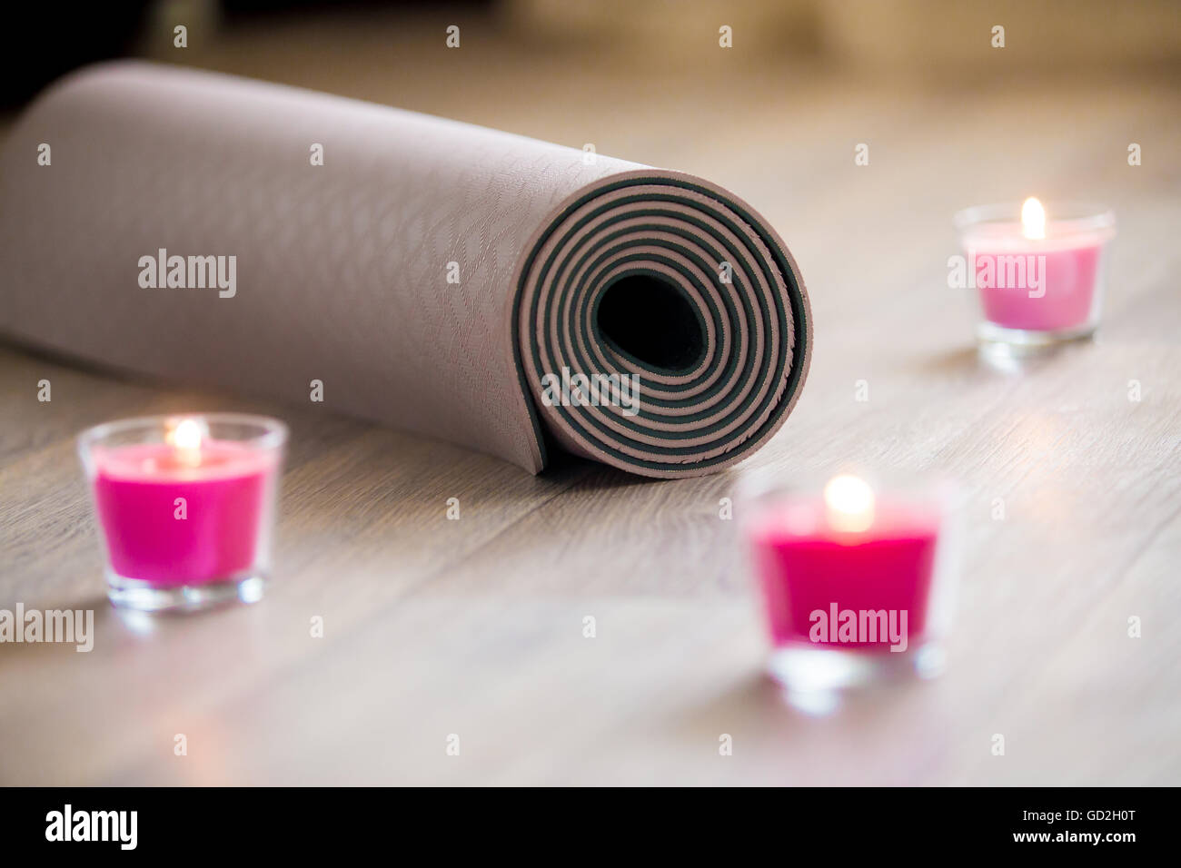 Rose-colored lighted pink wax candle and rolled brown yoga, pilates mat ...