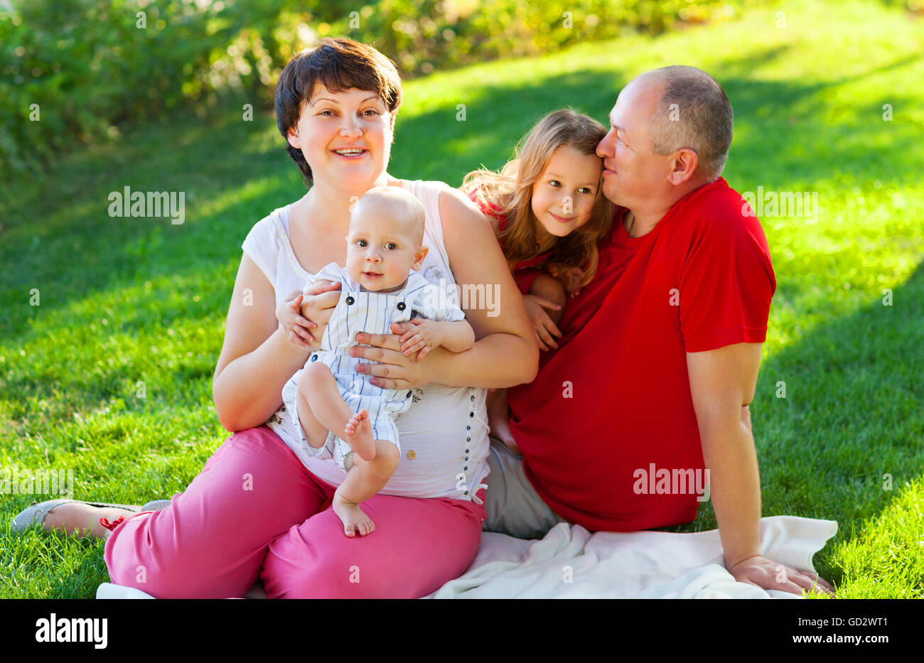 Happy family with two children sitting on green grass in the park Stock ...