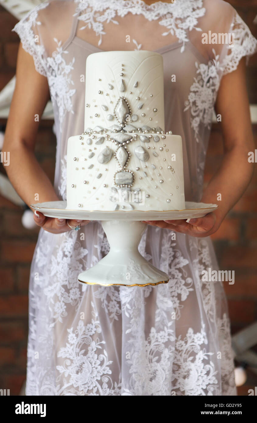Bride standing near the brick wall holding wedding cake. Close up Stock ...
