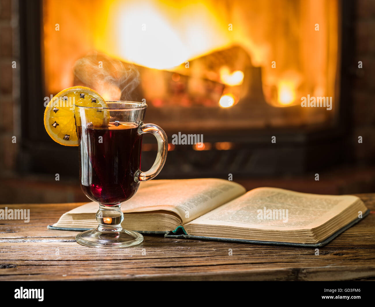 Hot mulled wine and a book on the wooden table. Fireplace with warm ...