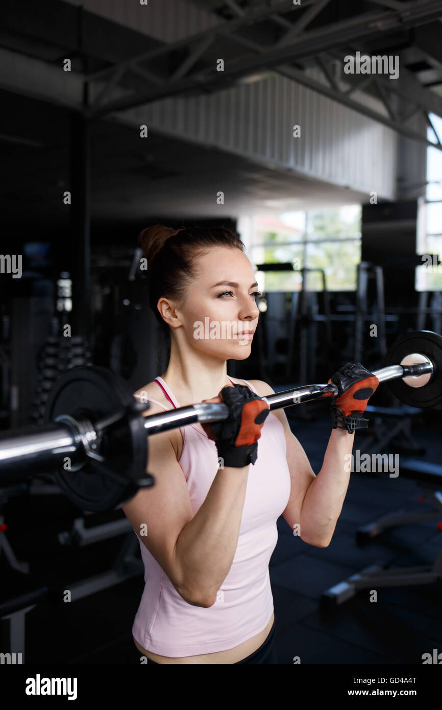 Young beautiful woman doing biceps curl with EZ curl bar in a gym ...