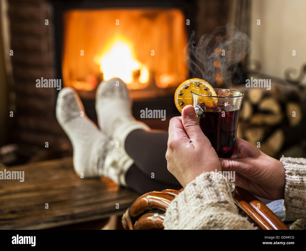 Hot mulled wine and book in woman hands. Relaxing in front of burning ...