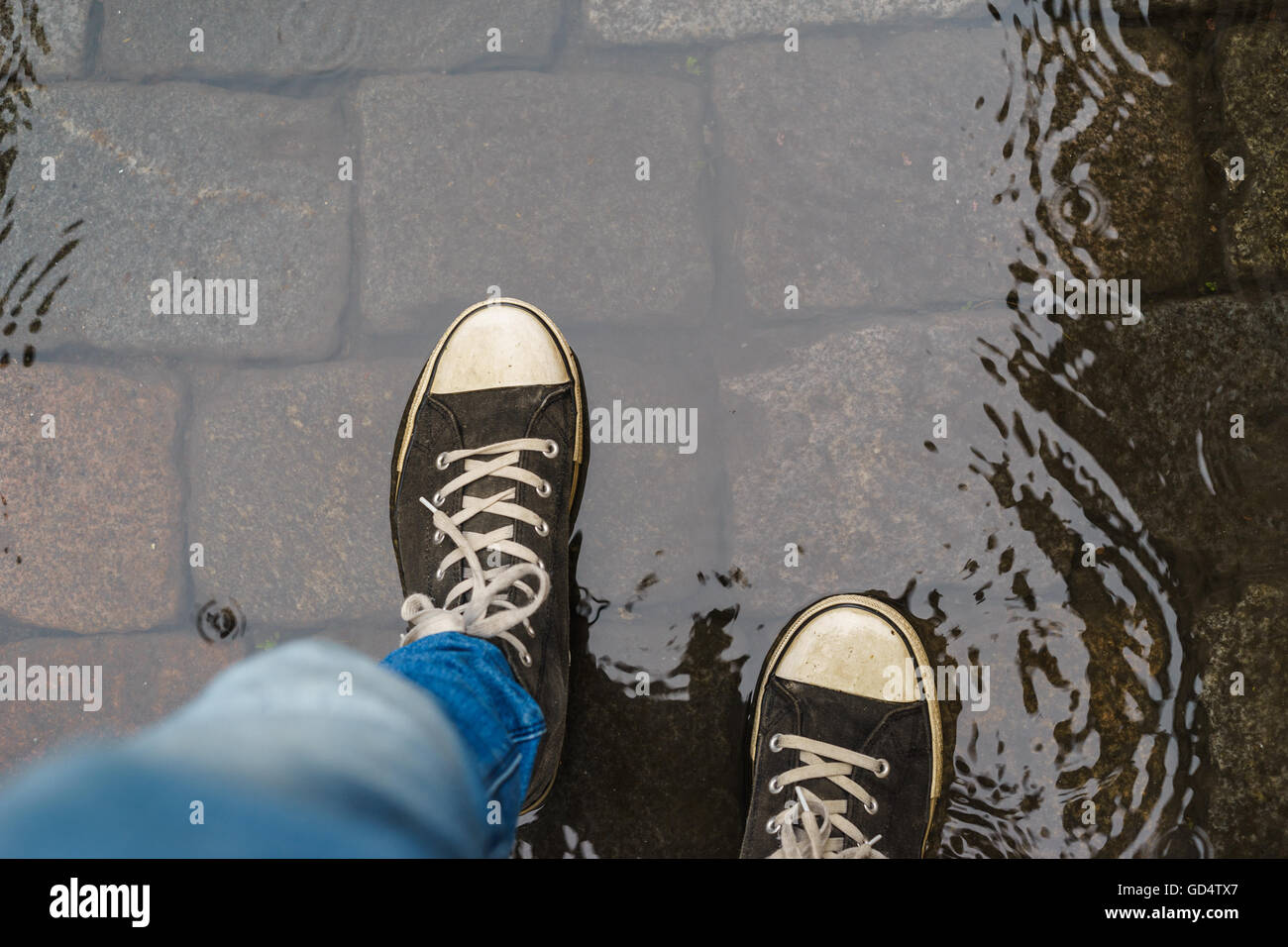 Male legs in sneakers and blue jeans walking through the rain puddle ...