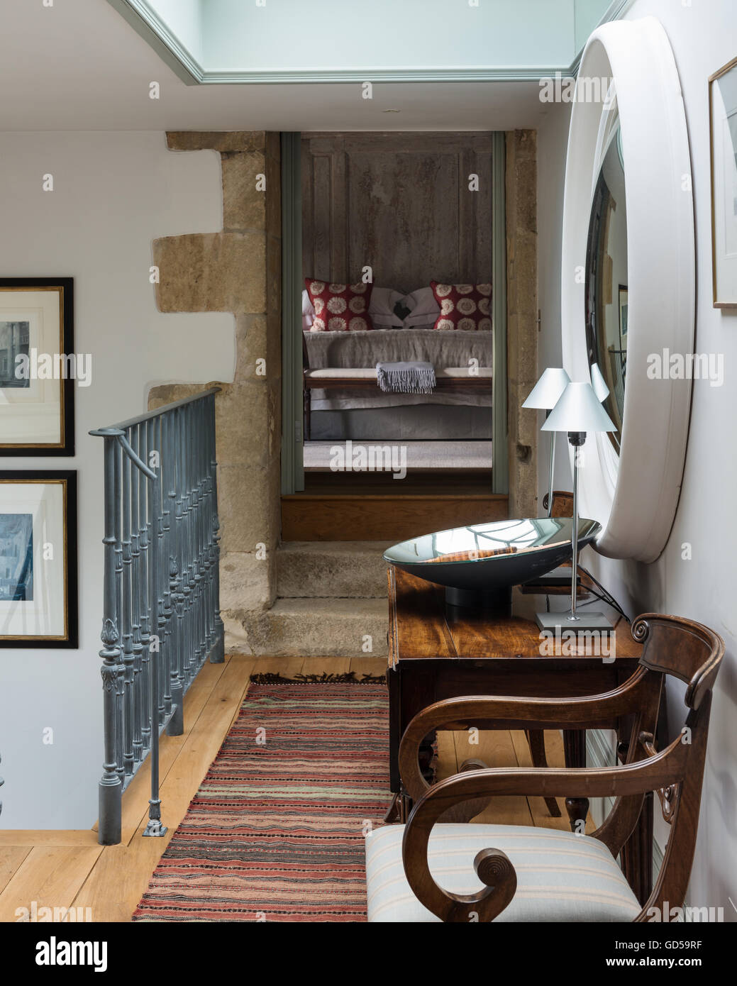 Oversized round mirror on landing with metal banisters and stone ...