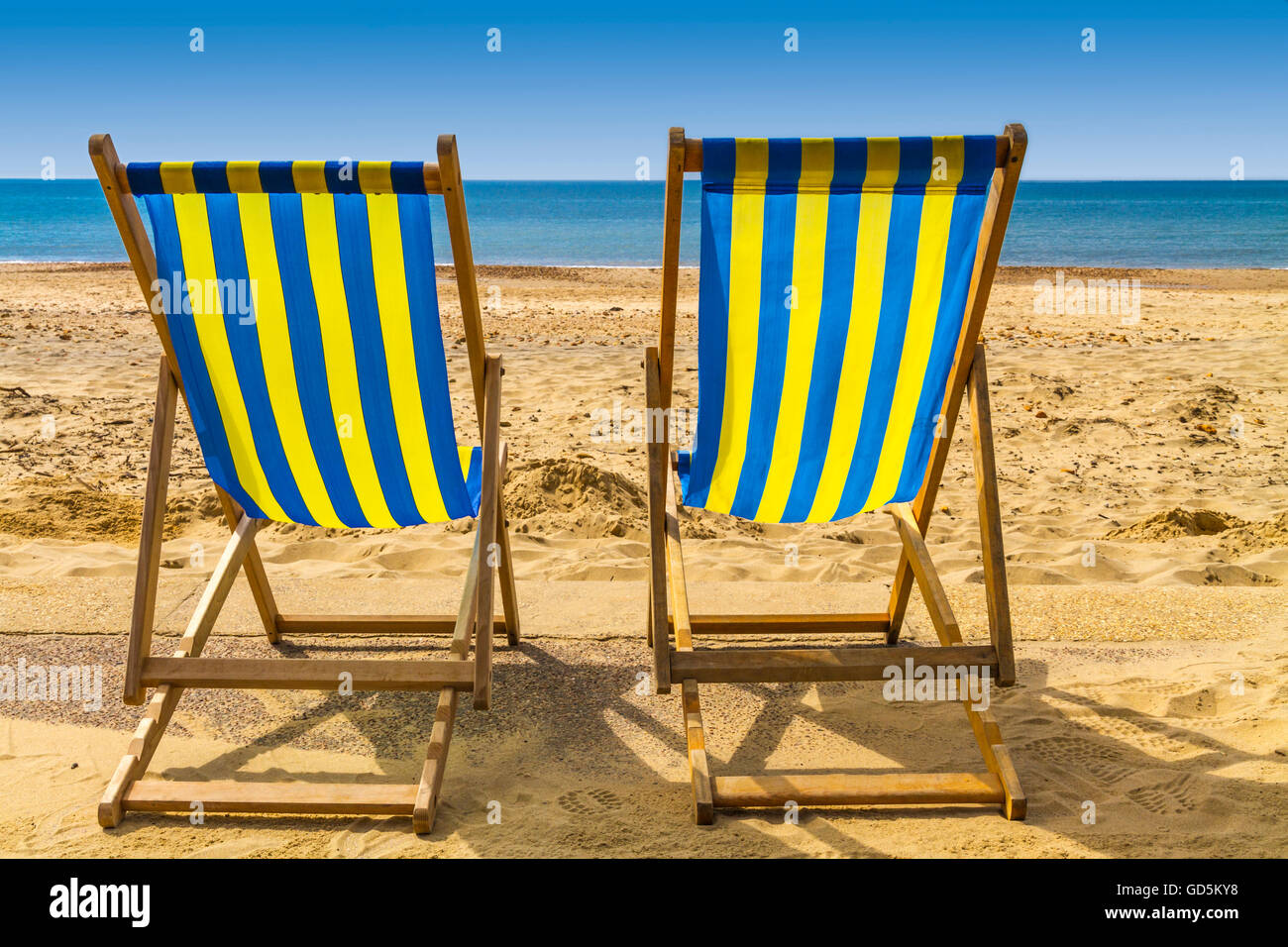 Two blue and yellow deck chairs facing the sea across golden sand on a ...
