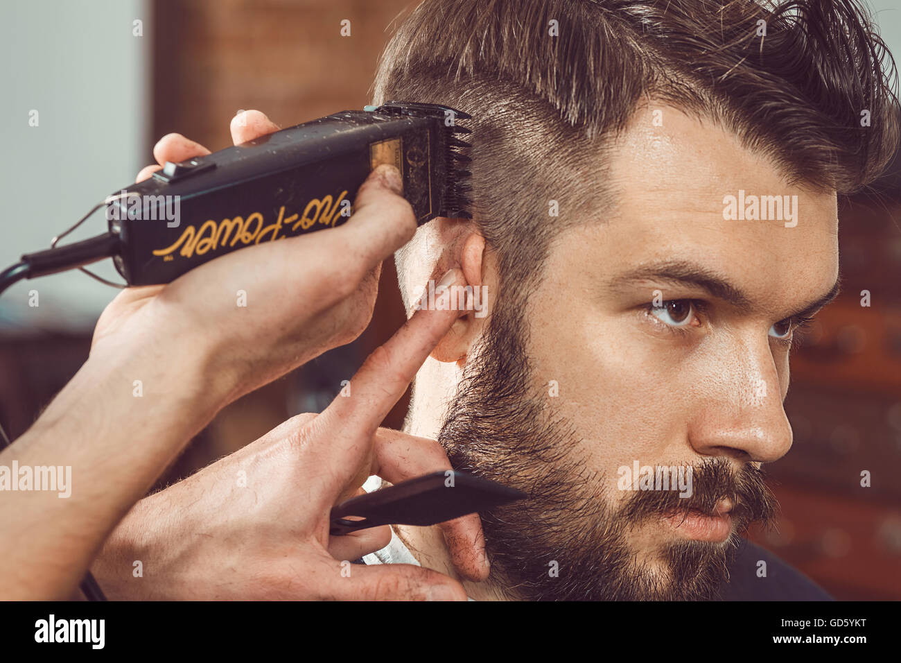 The hands of young barber making haircut to attractive man in ...