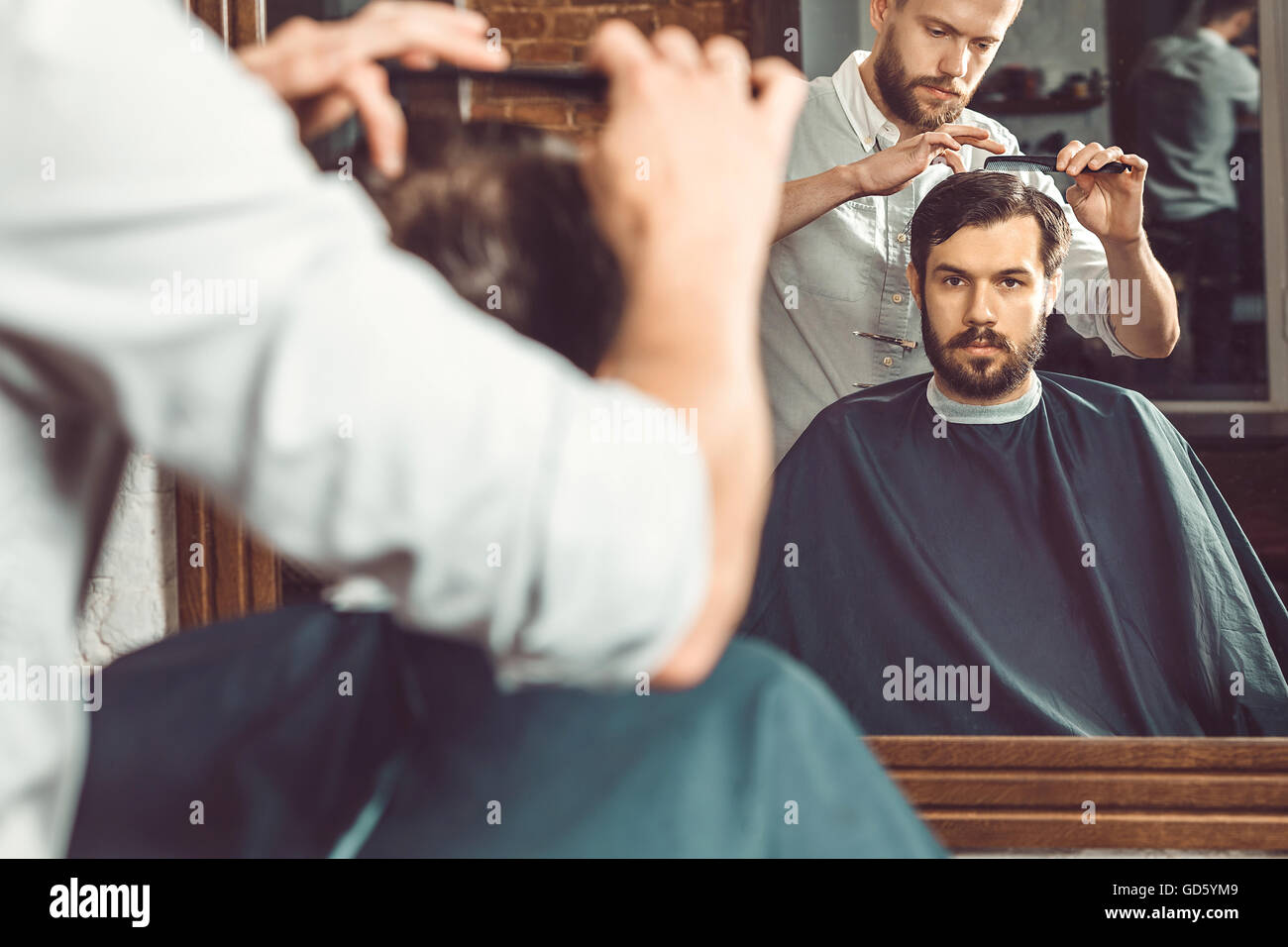 Young handsome barber making haircut of attractive man in barbershop ...