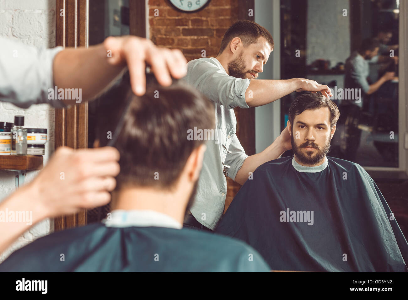Young handsome barber making haircut of attractive man in barbershop ...
