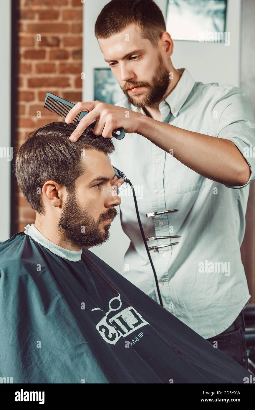 Young handsome barber making haircut of attractive man in barbershop ...