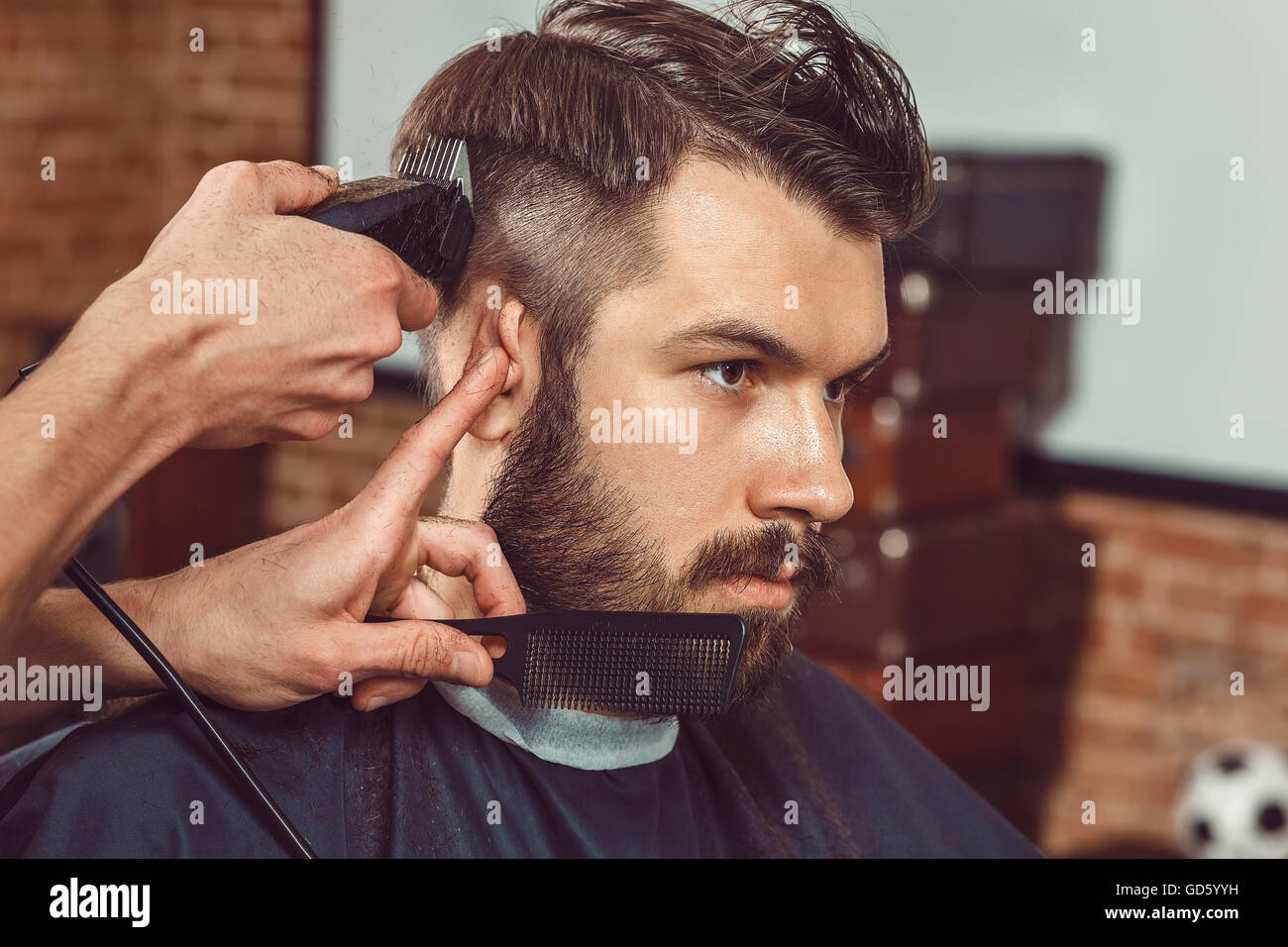 The hands of young barber making haircut to attractive man in ...