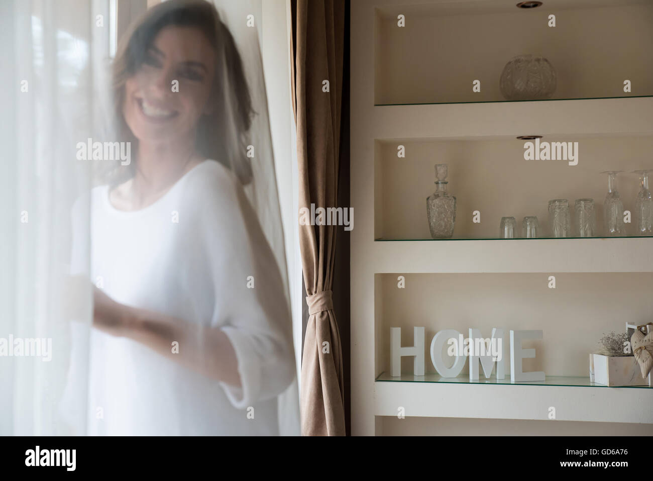 A beautiful young woman standing in the window behind the curtain and ...